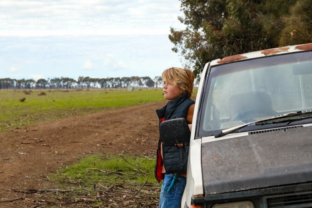 Image of Country boy leaning against old farm ute in paddock - Austockphoto
