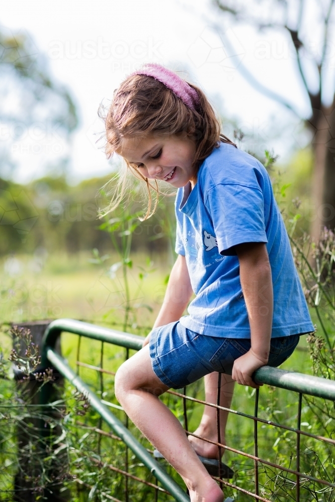 Image of Country kid climbing over farm gate - Austockphoto