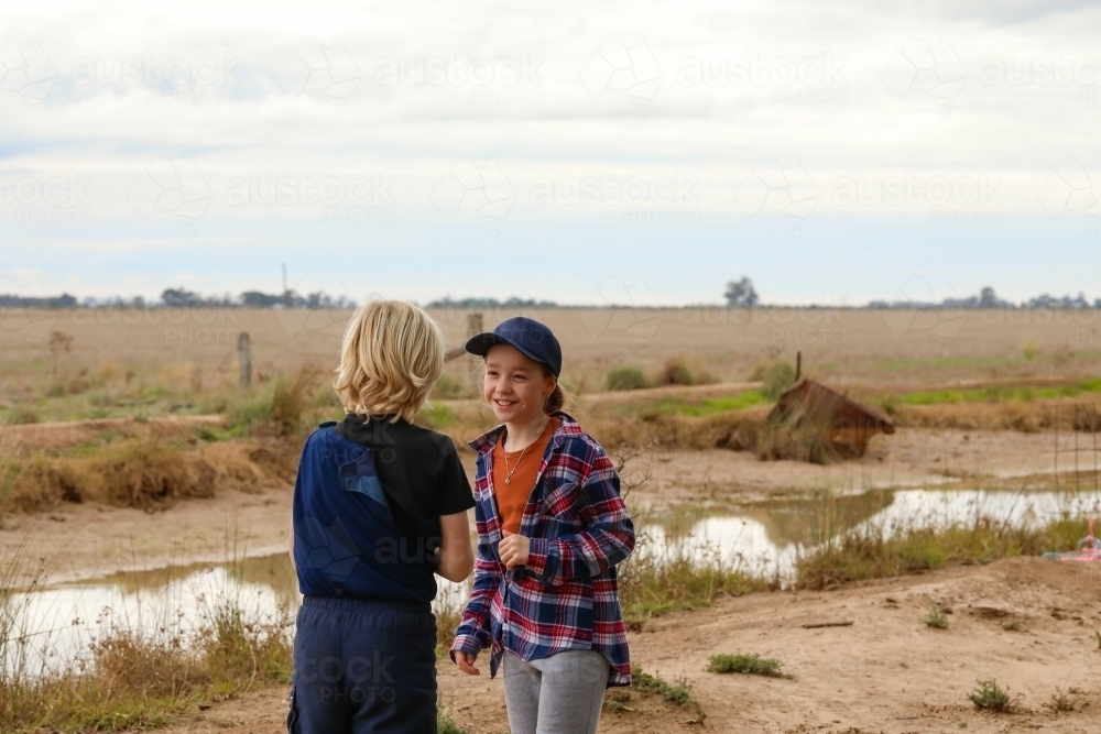 Image of Country kids chatting on channel bank on farm - Austockphoto
