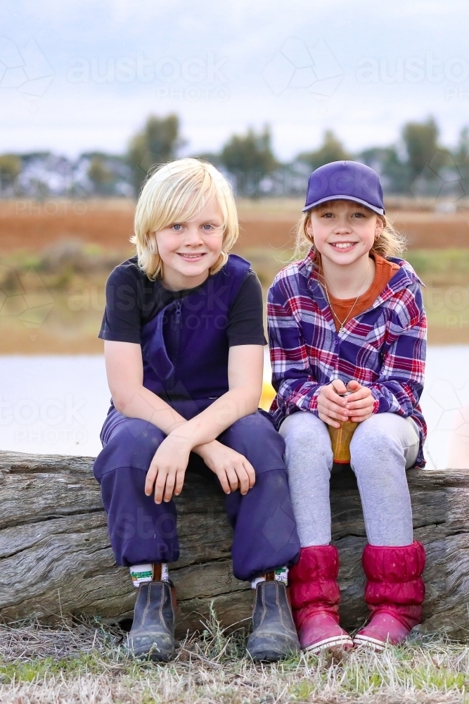 Image of Country kids sitting on log on farm with dam in background ...