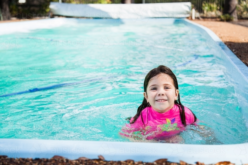 Image of Cute young girl swimming in backyard in ground pool - Austockphoto
