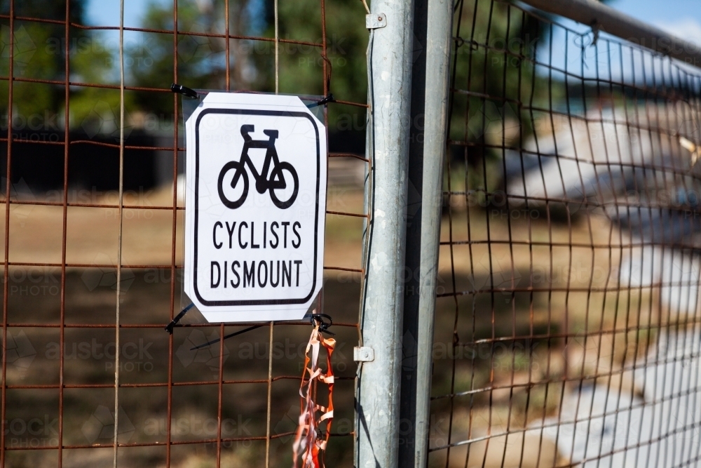 Image of Cyclists dismount sign on fence near construction site ...