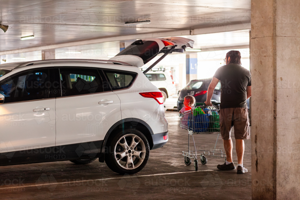 Image of dad pushing trolley in undercover carpark with toddler girl ...