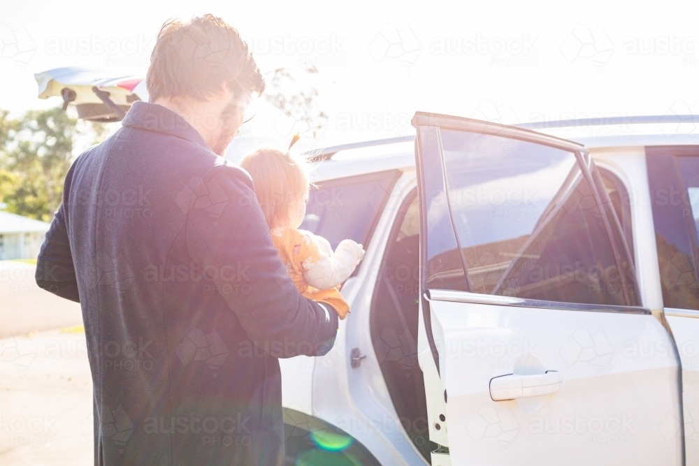 Image of Dad putting baby girl in car with sun flare light - Austockphoto