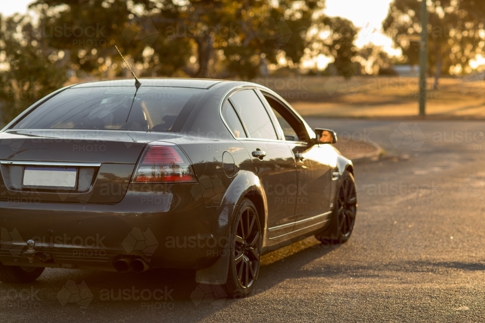 Image of Dark sedan car driving on quiet road with trees - Austockphoto