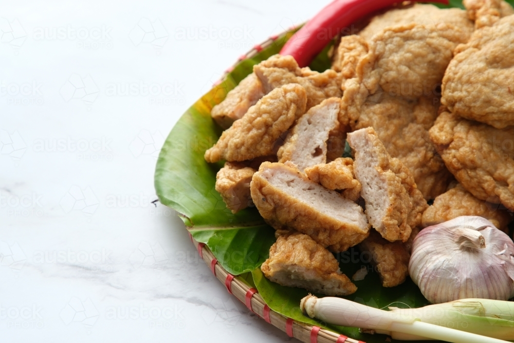 Image of Deep fried Cha Lua slices served on a banana leaf in a woven ...