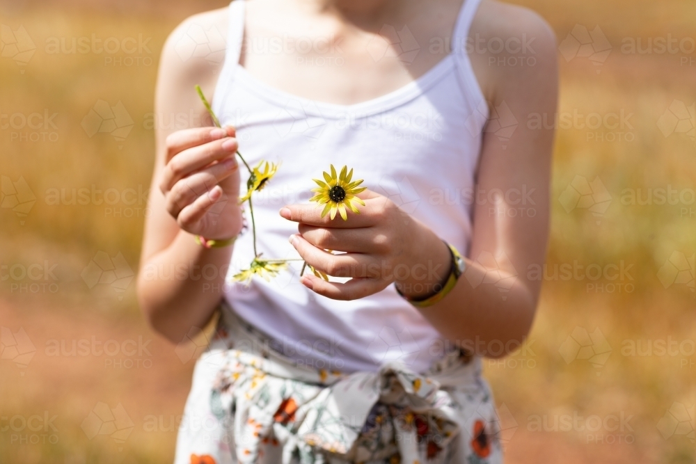 Image of detail of anonymous child wearing singlet making daisy chain ...
