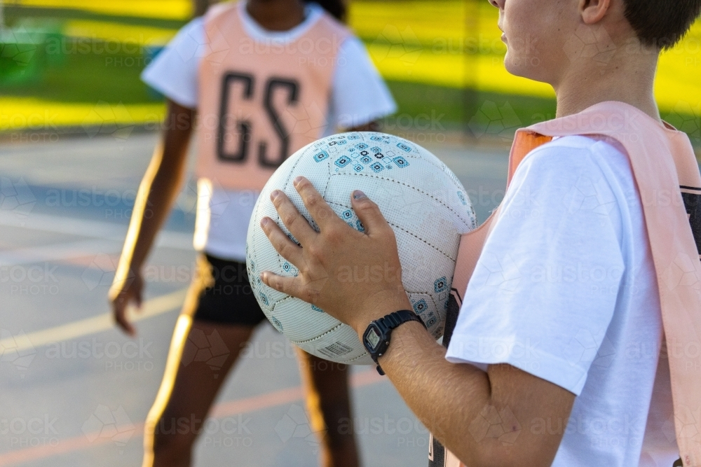 Image of detail of child holding netball with unidentified teammate ...