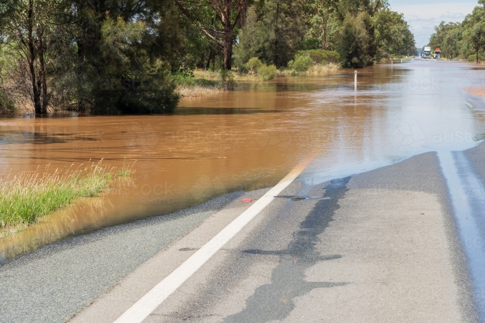 Image of Dirty flood waters across a country road - Austockphoto