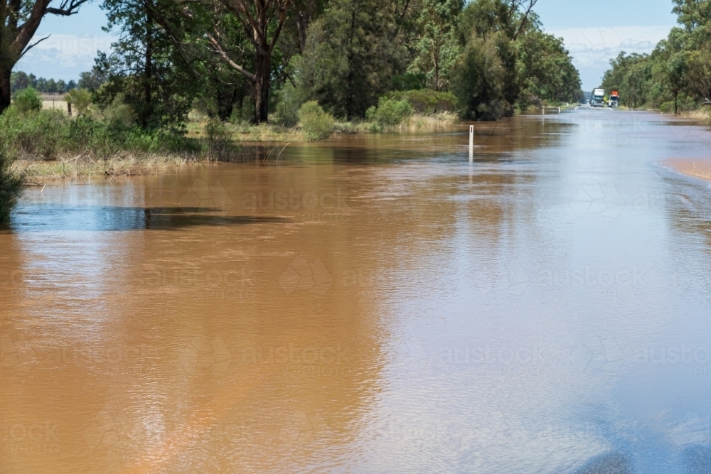 Image of Dirty flood waters across a country road - Austockphoto