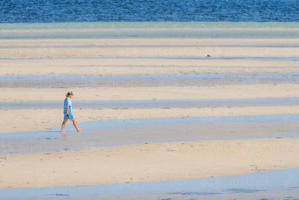 Image of Distant view of a lady walking on a wide sandy beach with ...