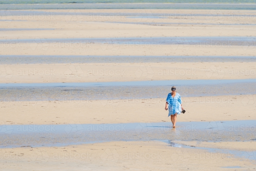 Image of Distant view of a lady walking on a wide sandy beach with ...