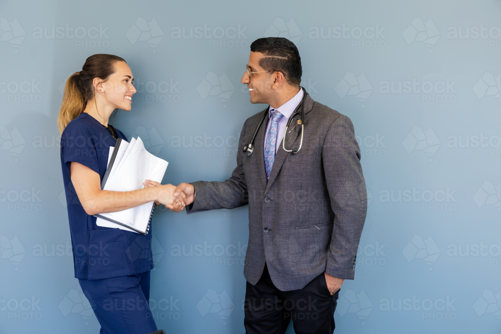 Image of Doctor and nurse shaking hands against blue wall - Austockphoto