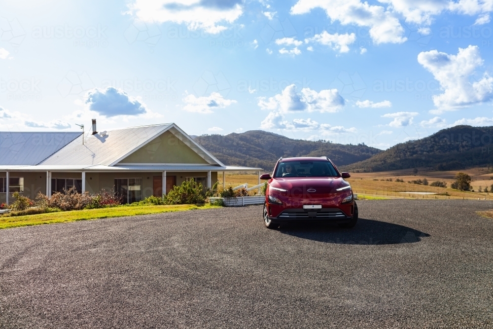 Image of Driving red electric vehicle past country farm house on ...