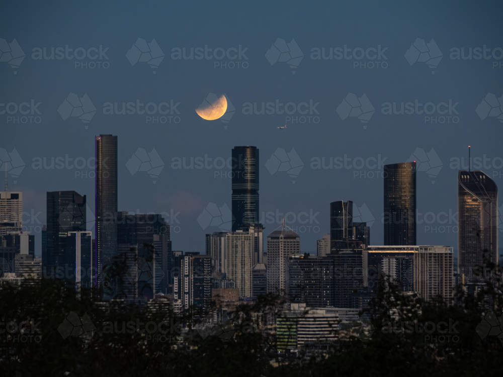 Image of Eclipse of the full moon shining over city skyline - Austockphoto