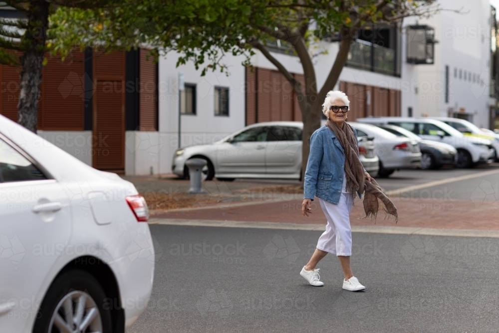 Image of elderly lady walking across street with parked cars and ...
