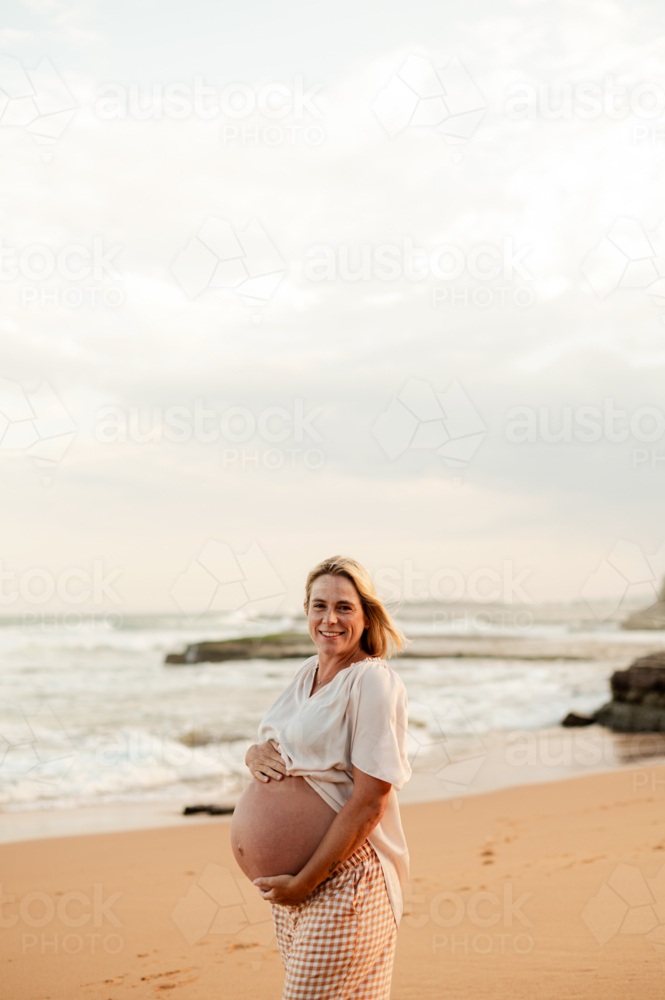 Image of Expecting mother smiling on beach at sunset, ocean waves in ...