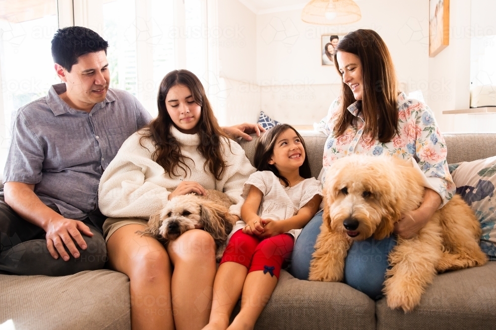 Image of Family of four sitting on the couch with their two pet dogs in ...