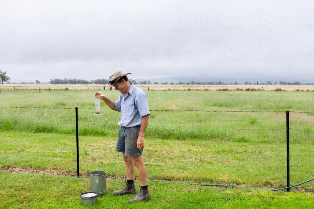 Image of farmer checking rainfall as rain storm finishes - Austockphoto