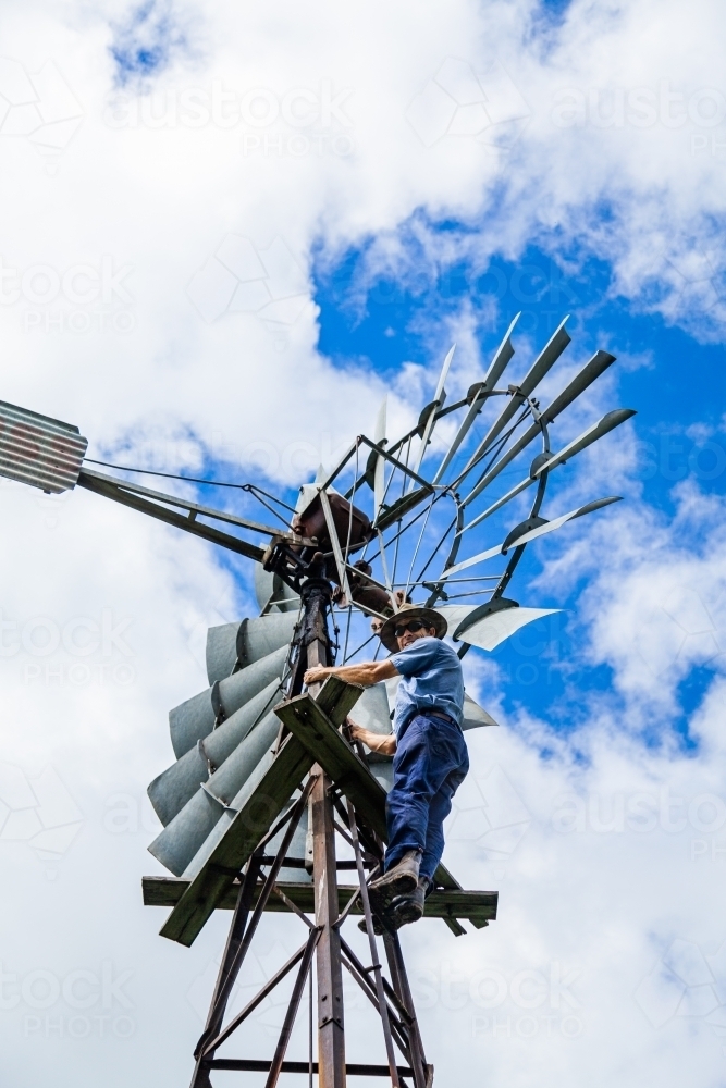 Image of Farmer climbing up farm windmill to check and repair pump ...