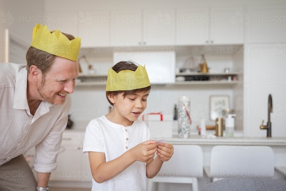Image of Father and son wearing yellow crowns reading Christmas cracker ...