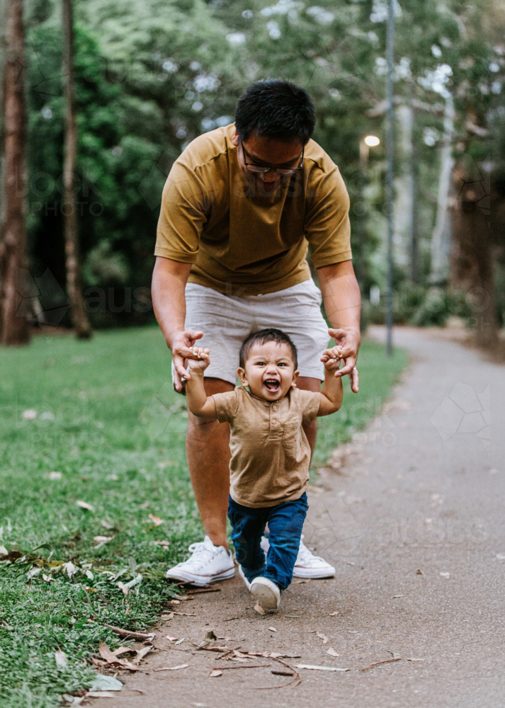 Image of Father helping baby boy walk at the park. - Austockphoto