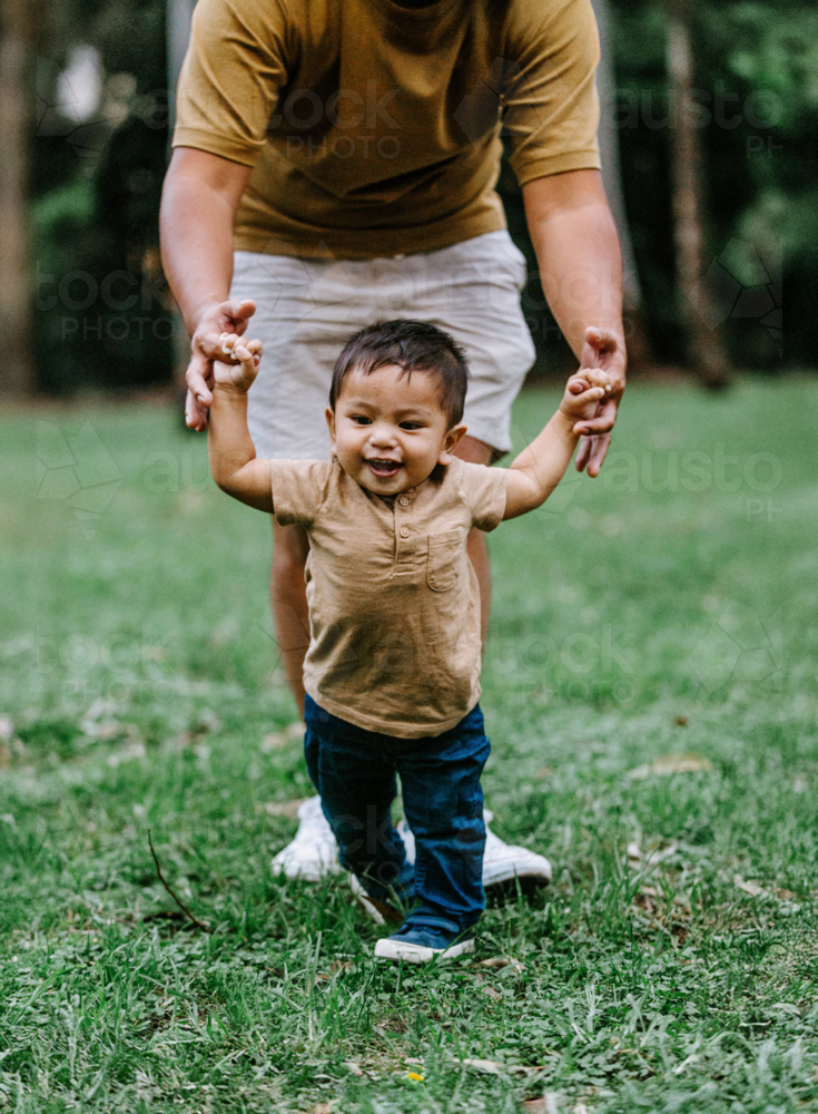 Image of Father helping baby boy walk at the park. - Austockphoto