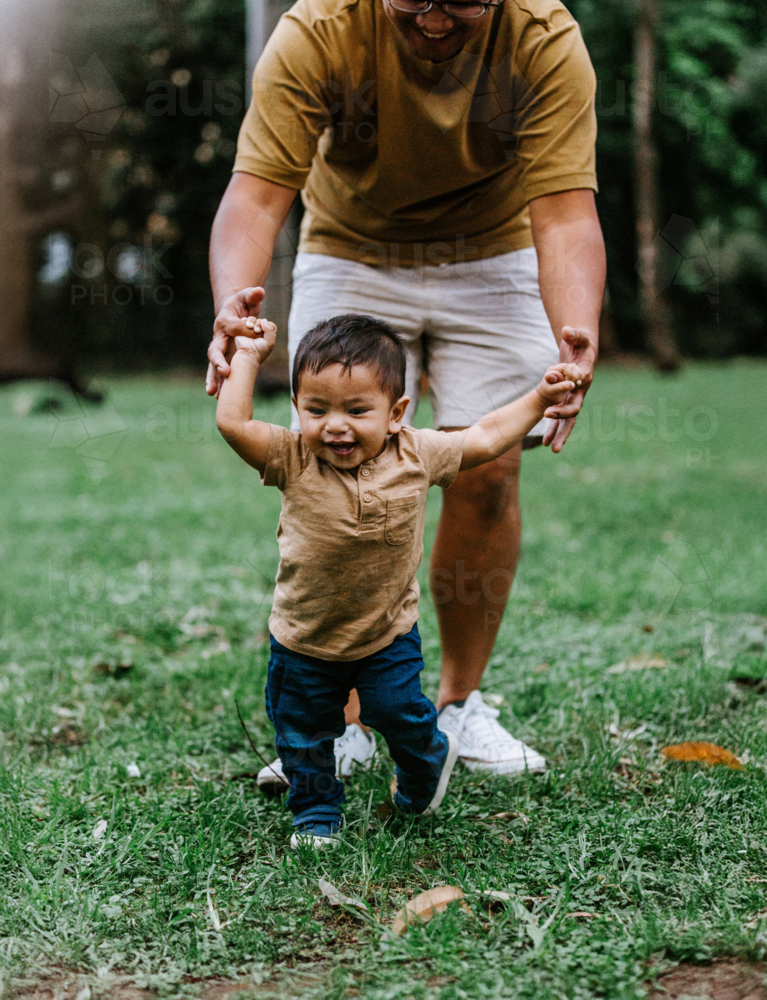 Image of Father helping baby boy walk at the park. - Austockphoto