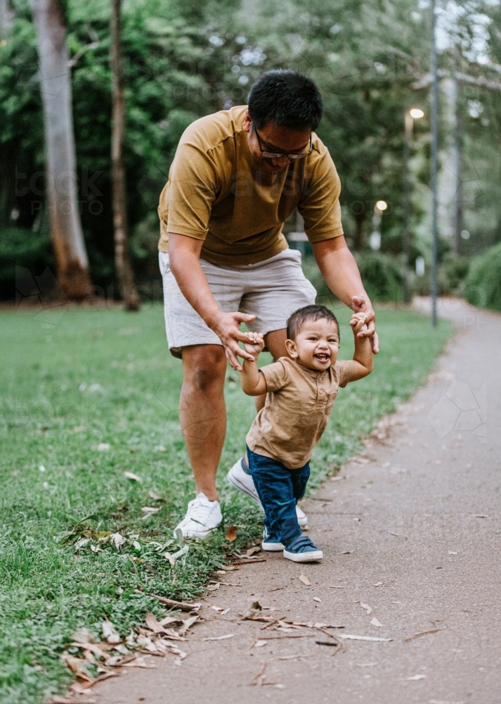 Image of Father helping baby boy walk at the park. - Austockphoto