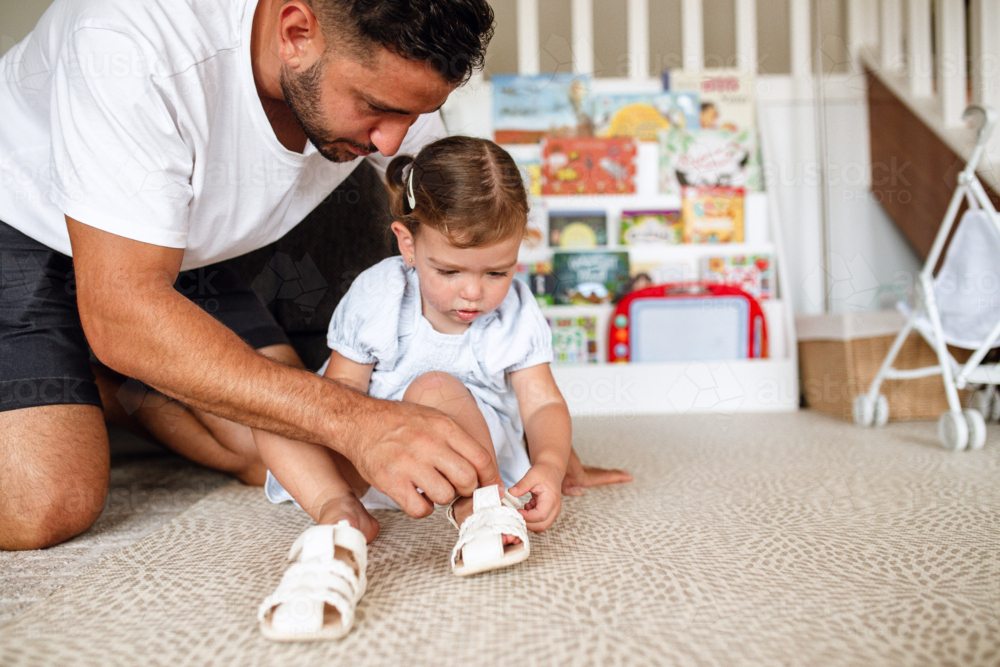 Image of Father helping toddler daughter put on her shoes - Austockphoto