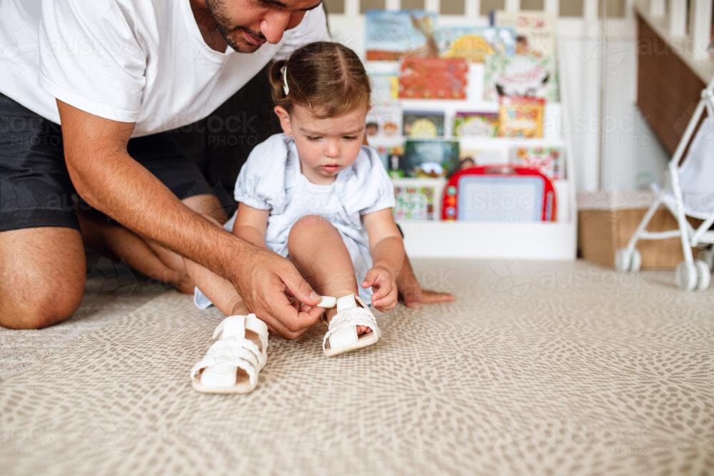 Image of Father helping toddler daughter put on her shoes - Austockphoto