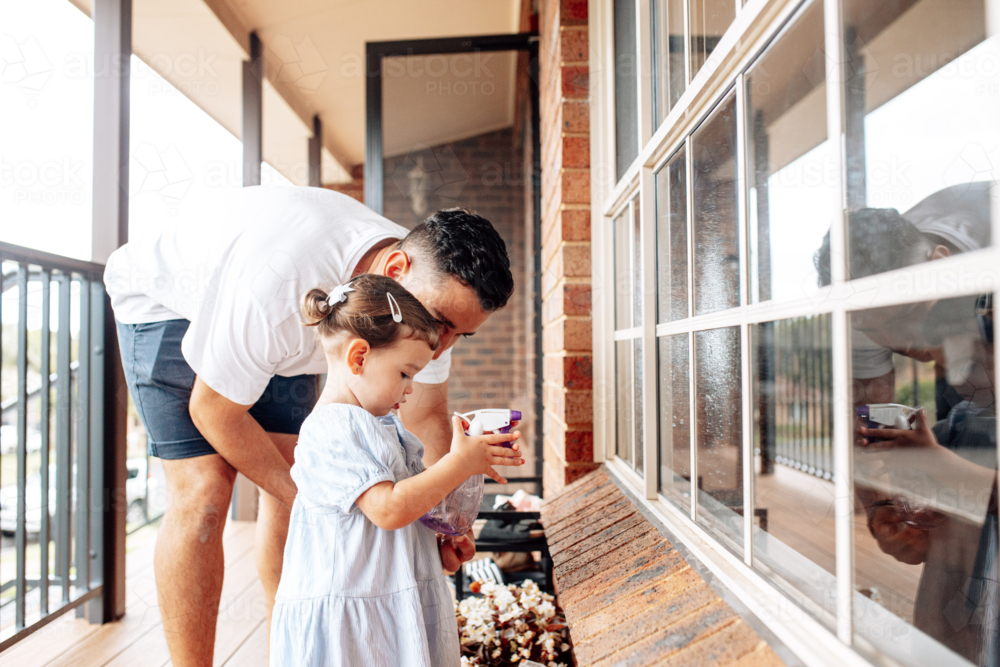 Image of Father helping toddler daughter with a spray bottle ...