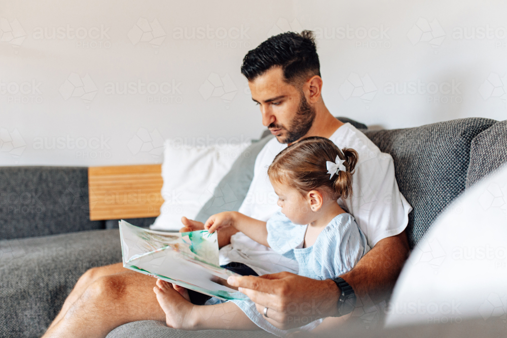 Image of Father reading story with toddler daughter on the couch ...
