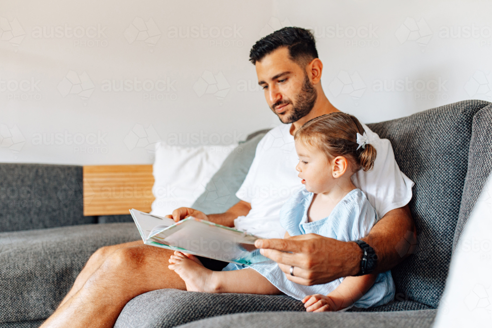 Image of Father reading story with toddler daughter on the couch ...