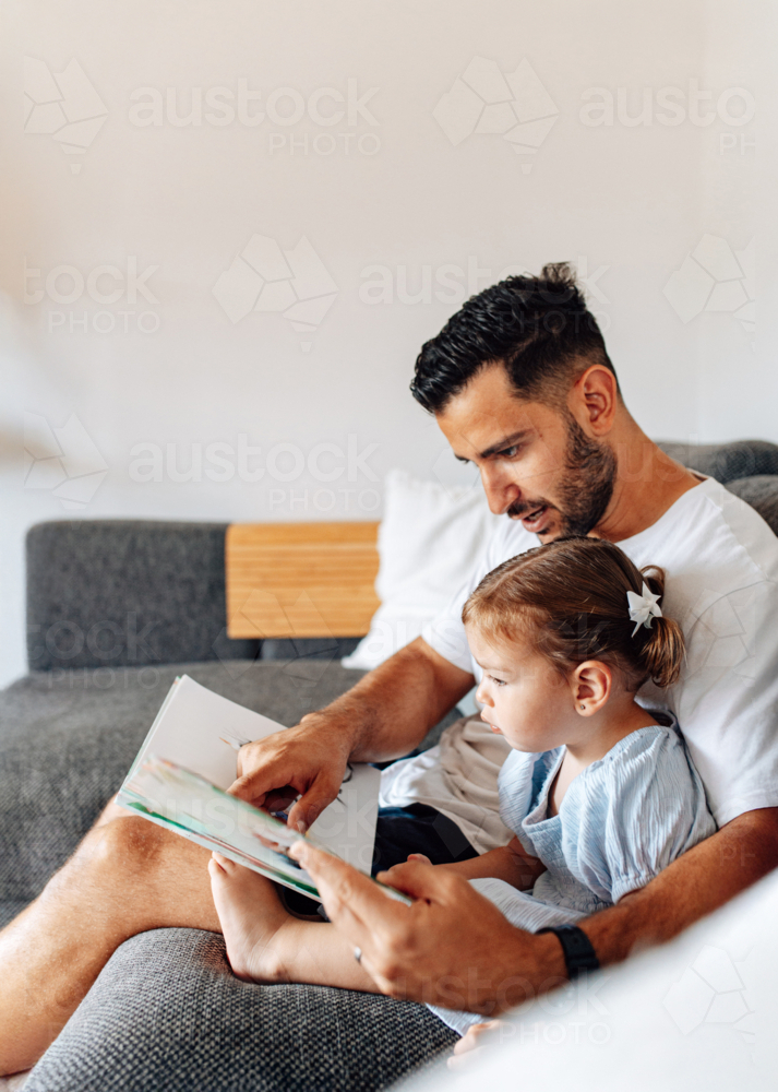 Image of Father reading story with toddler daughter on the couch ...