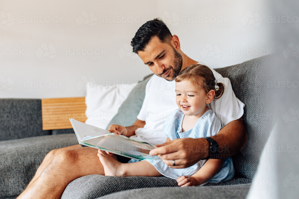 Image of Father reading story with toddler daughter on the couch ...