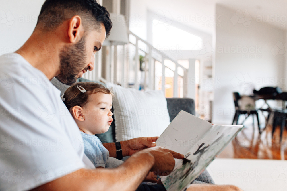 Image of Father reading story with toddler daughter on the couch ...