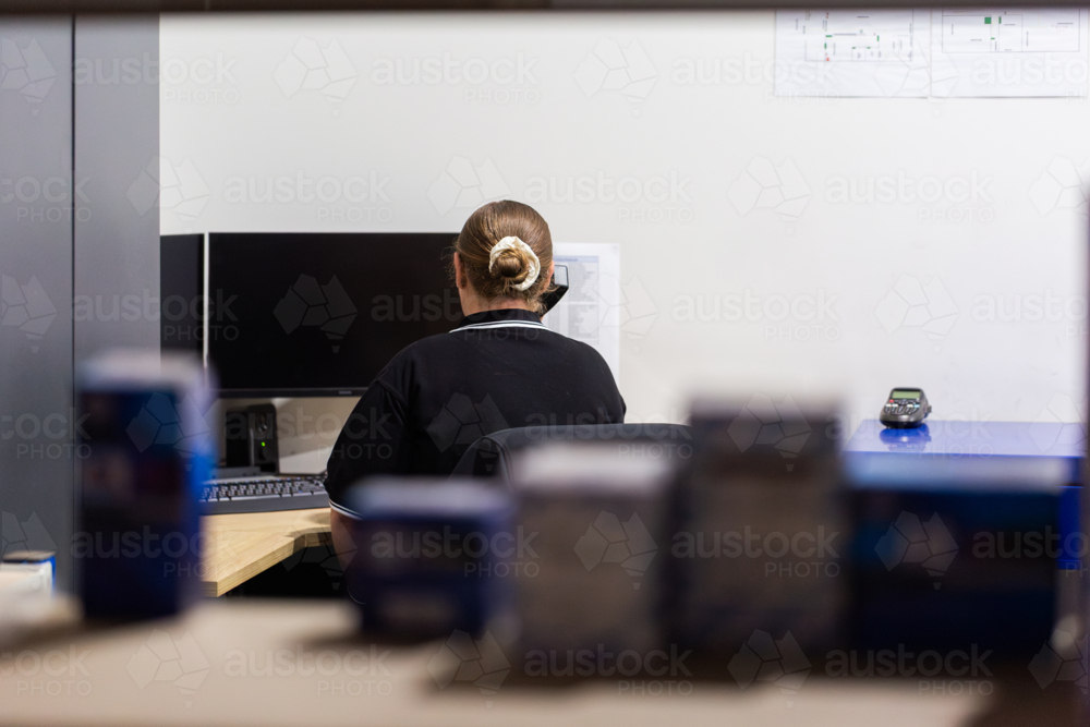 Image of Female office staff seated behind stockroom desk in front of ...
