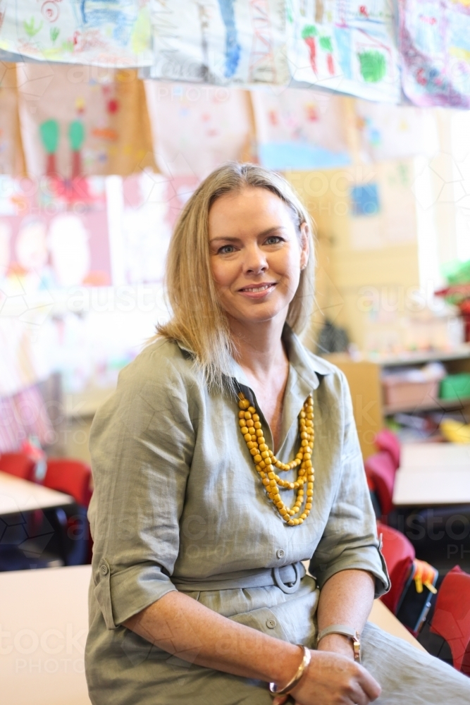 Image of Female teacher sitting on classroom desk smiling - Austockphoto