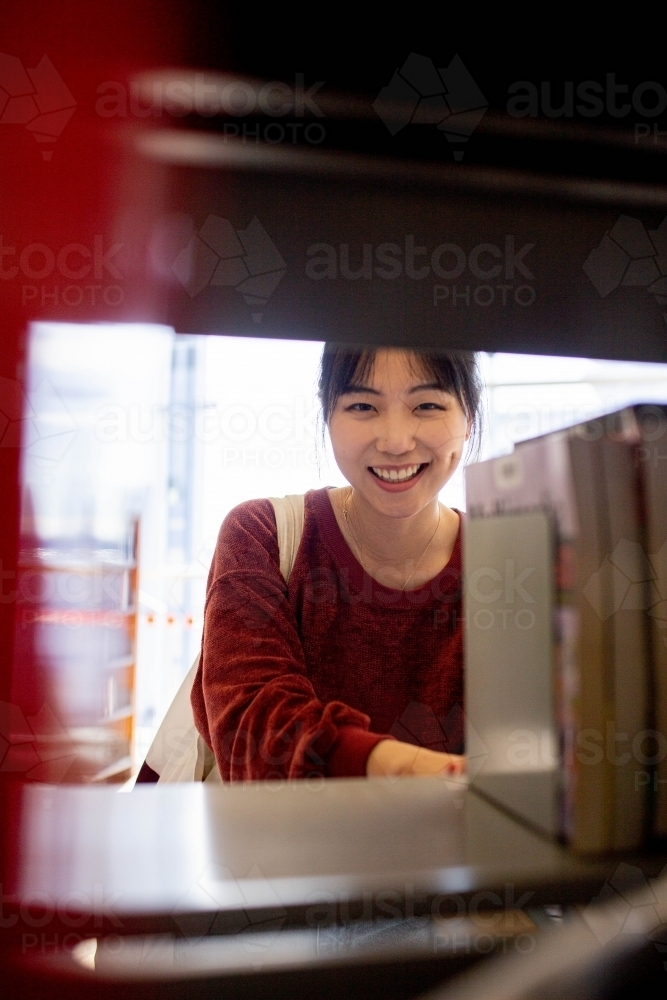 Image of Female university student looking through a bookcase ...