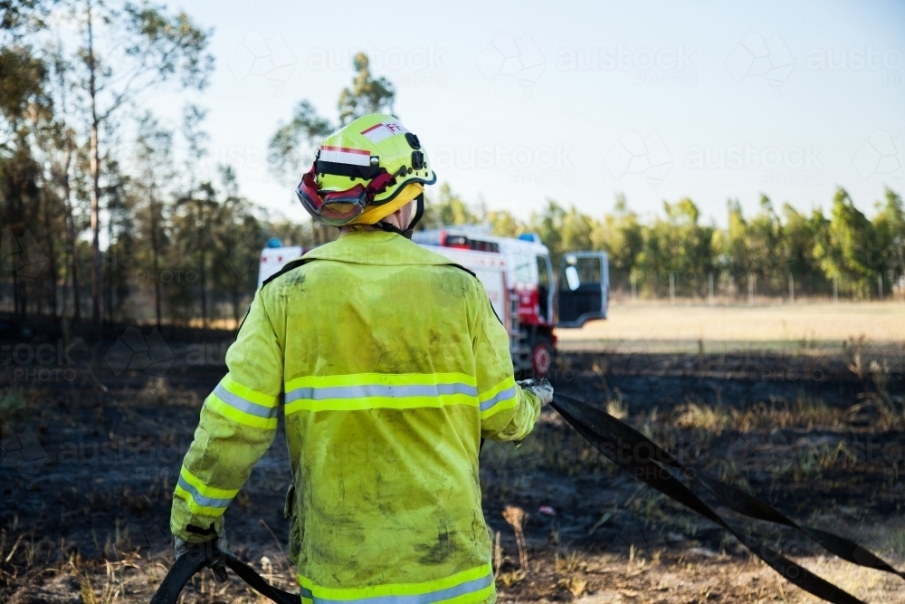 Image of Fire rescue workers pulling fire hose with burnt grass behind ...