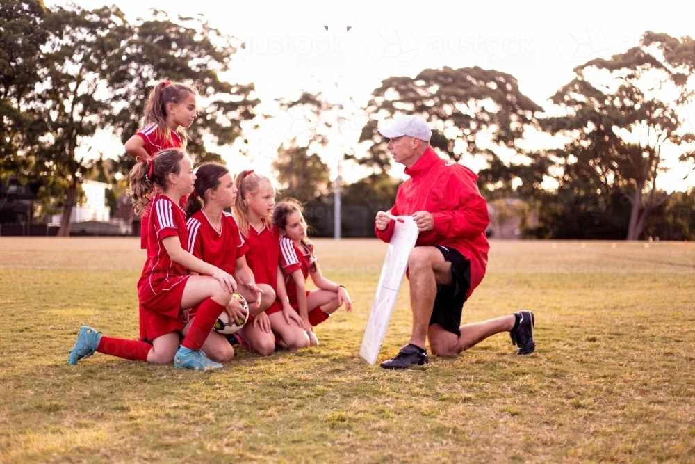 Image of Football coach explaining strategy to his team of tween girls ...