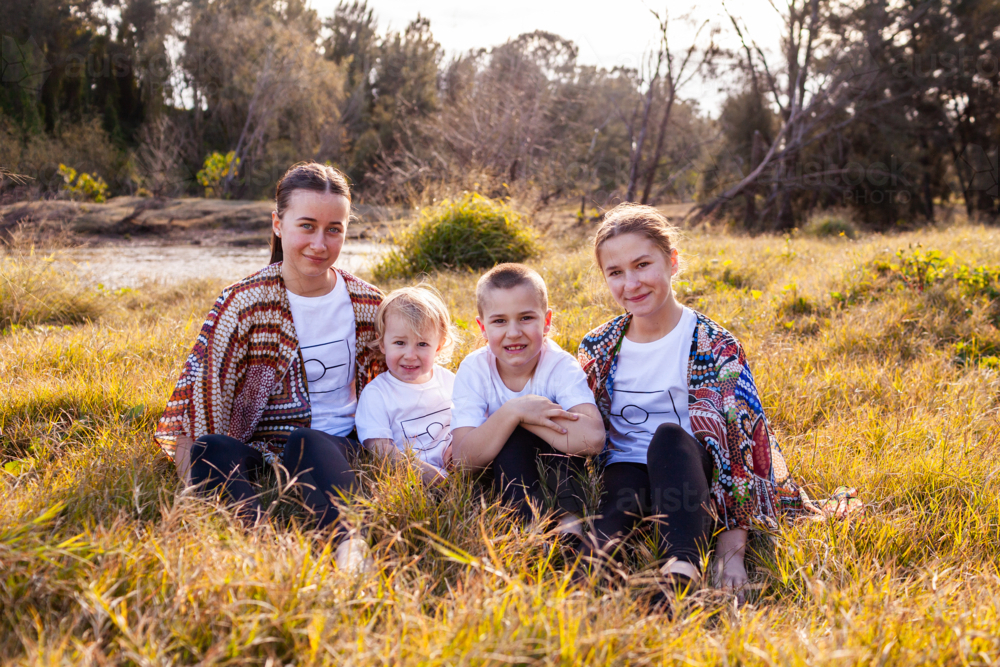 Image of Four aboriginal siblings sitting together in wild grassy area ...