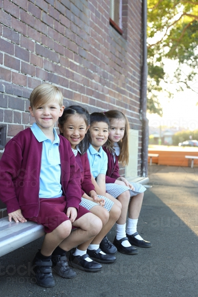 Image of Four smiling school children sitting on a school bench ...