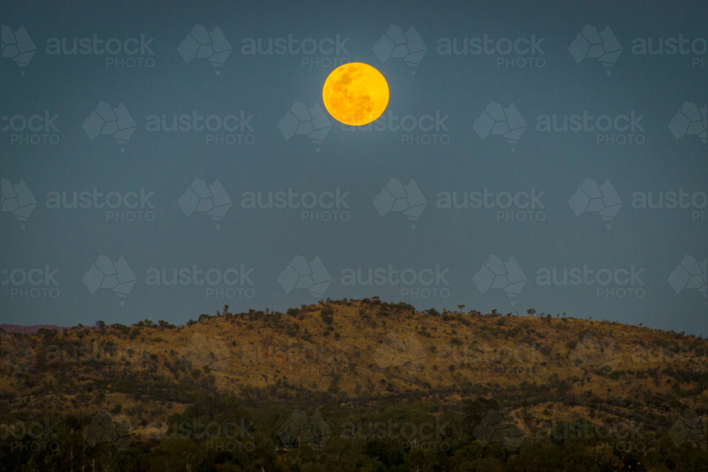 Image of Full moon rising over rugged hilltop in twilight sky ...