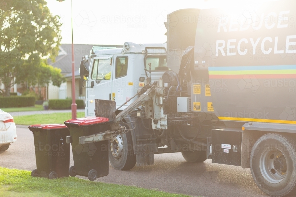 Image of Garbage truck picking up bins from curb side in suburban area ...