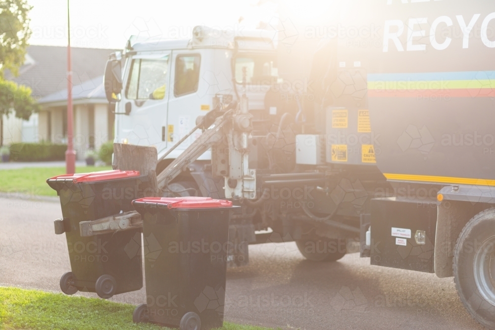 Image of Garbage truck picking up bins from curb side in suburban area ...