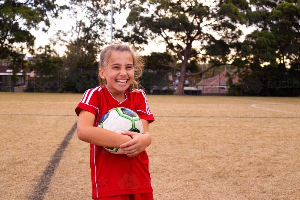Image of Girl in red soccer uniform laughing holding a ball - Austockphoto