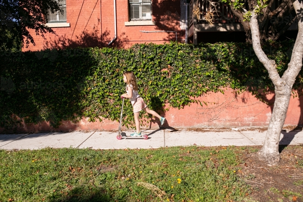 Image of girl riding on a scooter down the sidewalk with vines on the ...