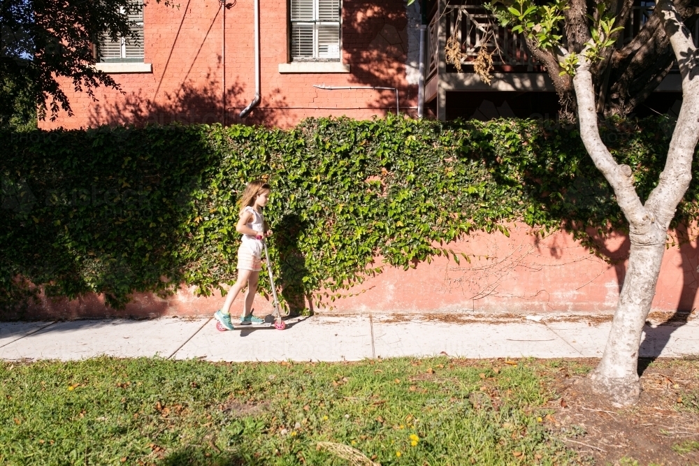 Image of girl riding on a scooter on the sidewalk with vines on wall ...